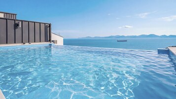 Piscina infinita com vista clara do mar e montanhas ao longe.