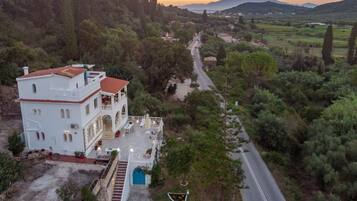 Uma villa branca com telhado de telhas vermelhas, um pátio pavimentado e uma escadaria que leva à entrada.