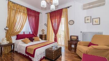 Quarto com cama, cómoda, mesa pequena, sofá e radiador.