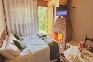 Quarto com cama, TV fixada em parede de tijolos e lareira.