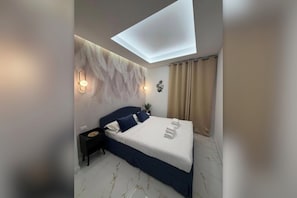 Quarto moderno com claraboia, cama com roupa de cama branca, mesa de cabeceira e luminária fixada na parede.