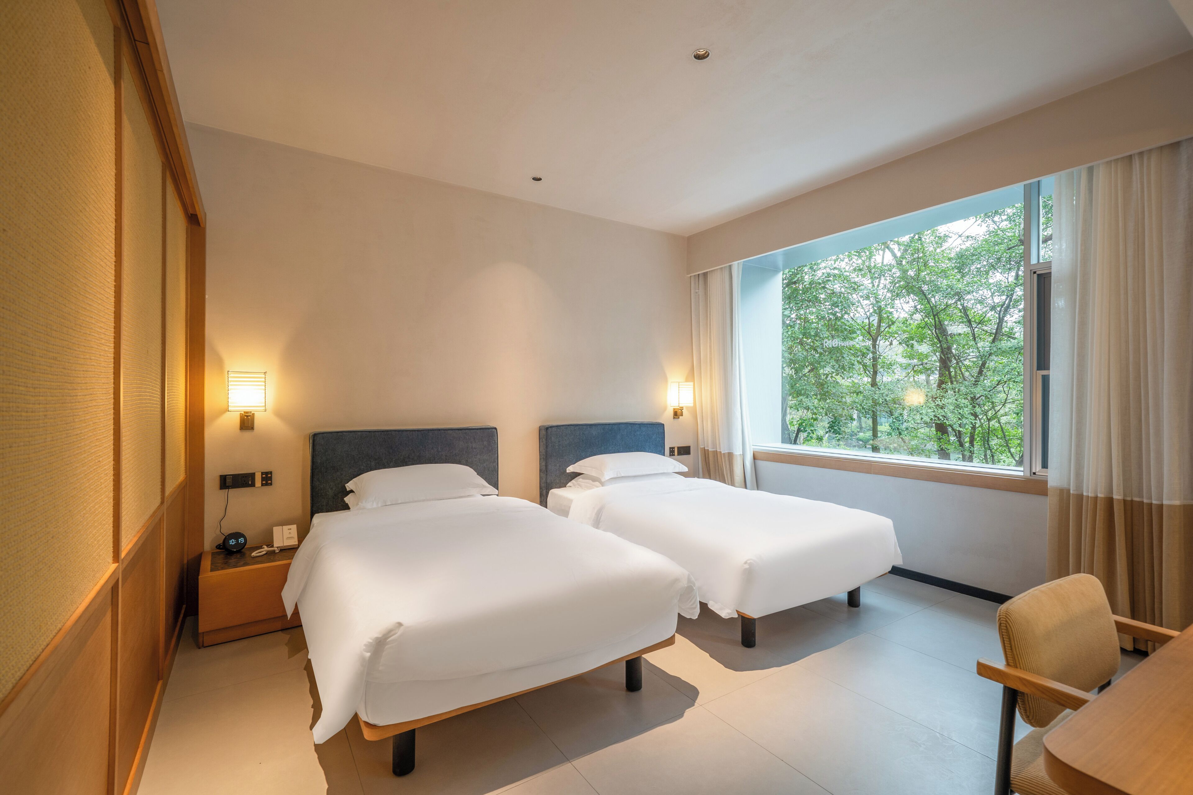 Quarto de hotel com duas camas, uma escrivaninha e uma cadeira.