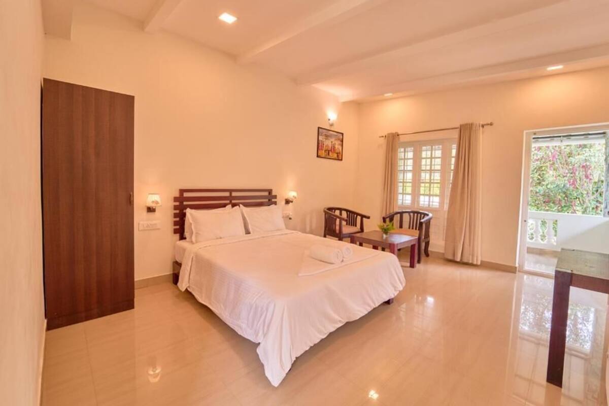 Quarto de hotel com cama, escrivaninha, cadeira, janela com cortinas e porta.