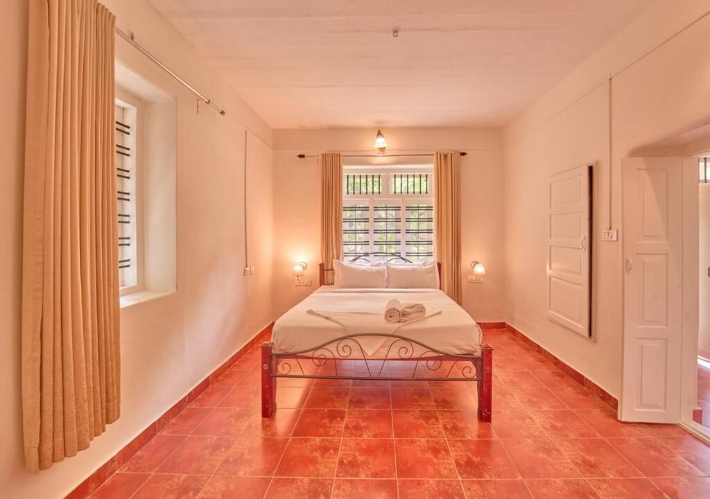 Quarto com cama, janela com cortinas, porta e luminária.