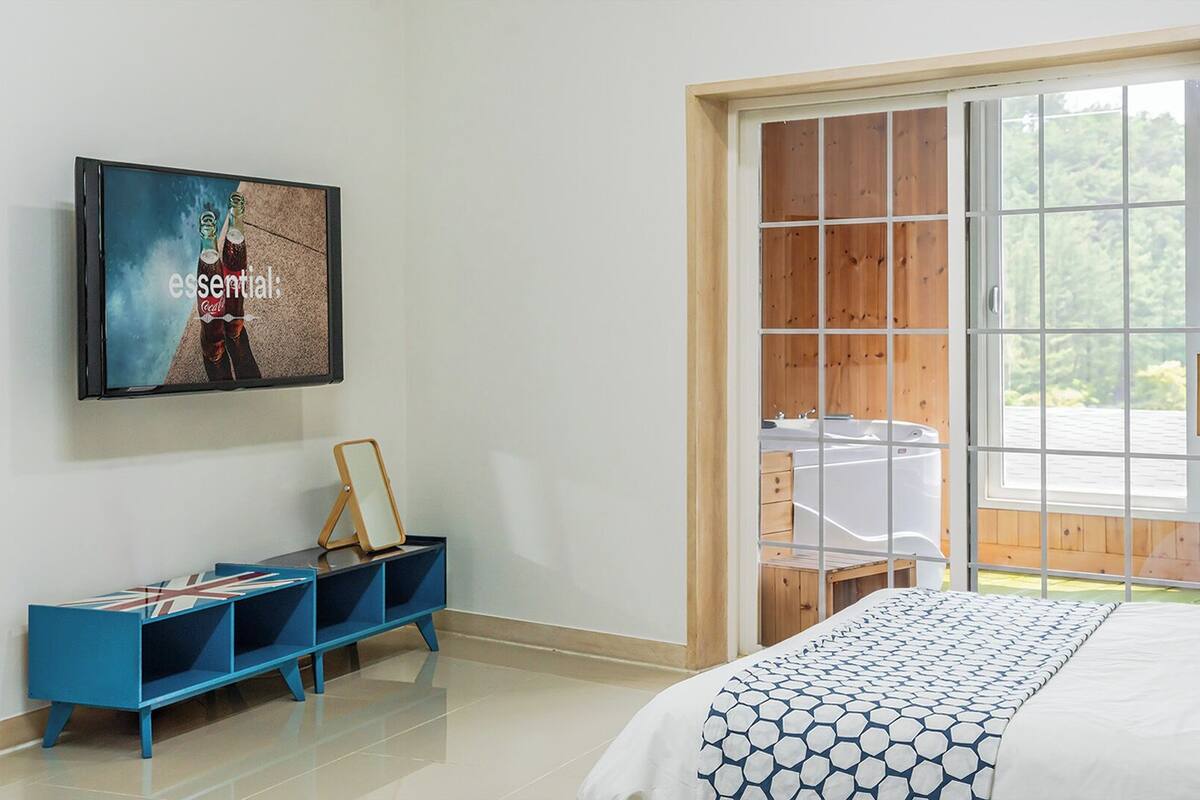 Quarto com uma cama, uma porta de madeira que dá para uma varanda, um móvel de armazenamento azul e um cartaz na parede.
