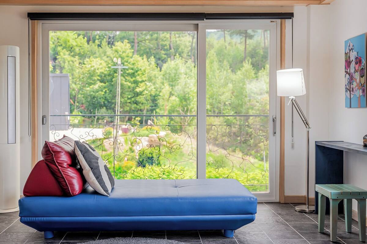 Um quarto com sofá azul, porta de vidro para um jardim, luminária de chão e um quadro na parede.