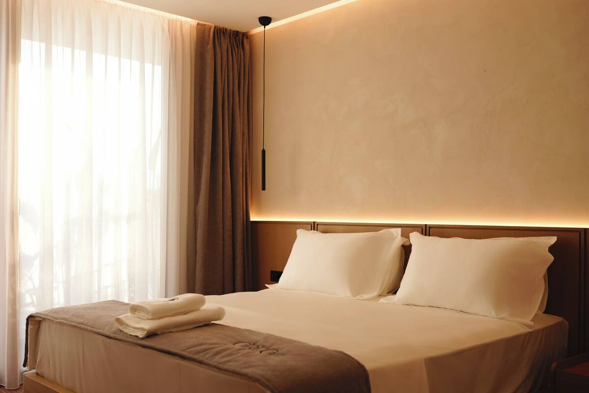 Quarto de hotel com cama, cortinas e luminária fixada na parede.