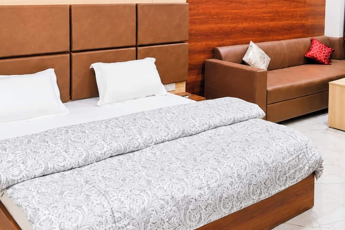 Quarto de hotel moderno com uma cama grande, cabeceira de madeira, sofá de couro marrom e uma parede de destaque em madeira.