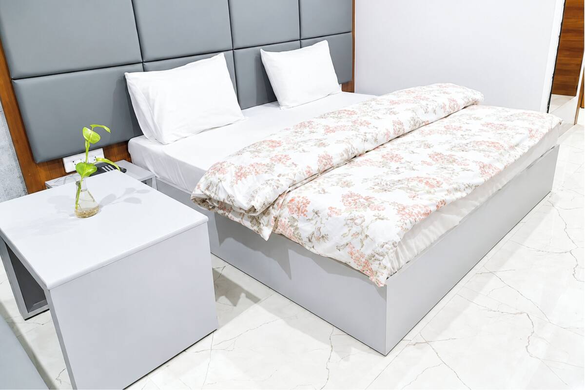 Quarto moderno com cabeceira cinza, roupa de cama branca, edredom floral e mesa de cabeceira com uma planta.