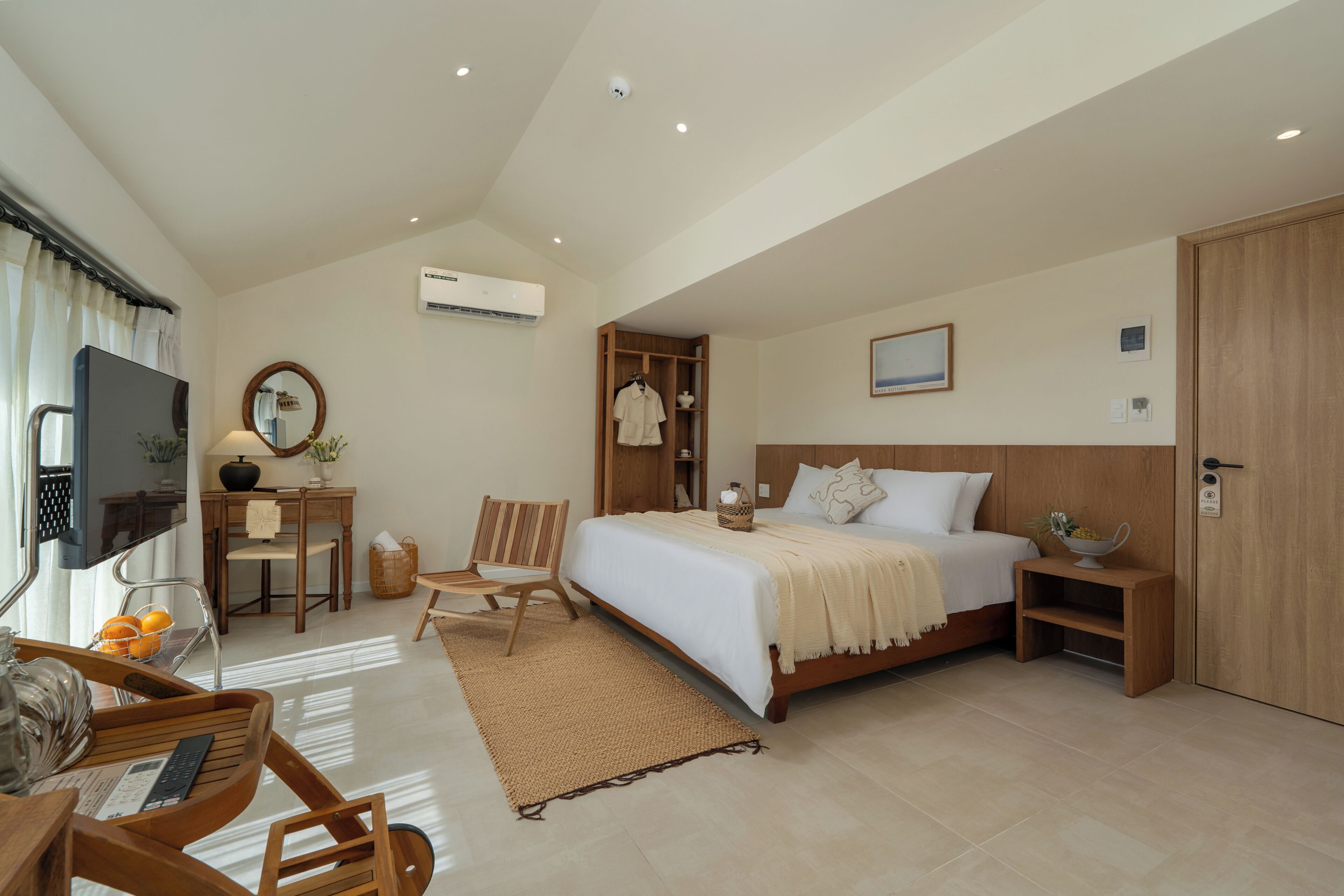 Quarto moderno com cama, mesas de cabeceira, televisão, escrivaninha e uma cadeira.