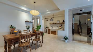 Uma sala de jantar espaçosa, com mesa e cadeiras de madeira, luminária pendente e vista para a cozinha.