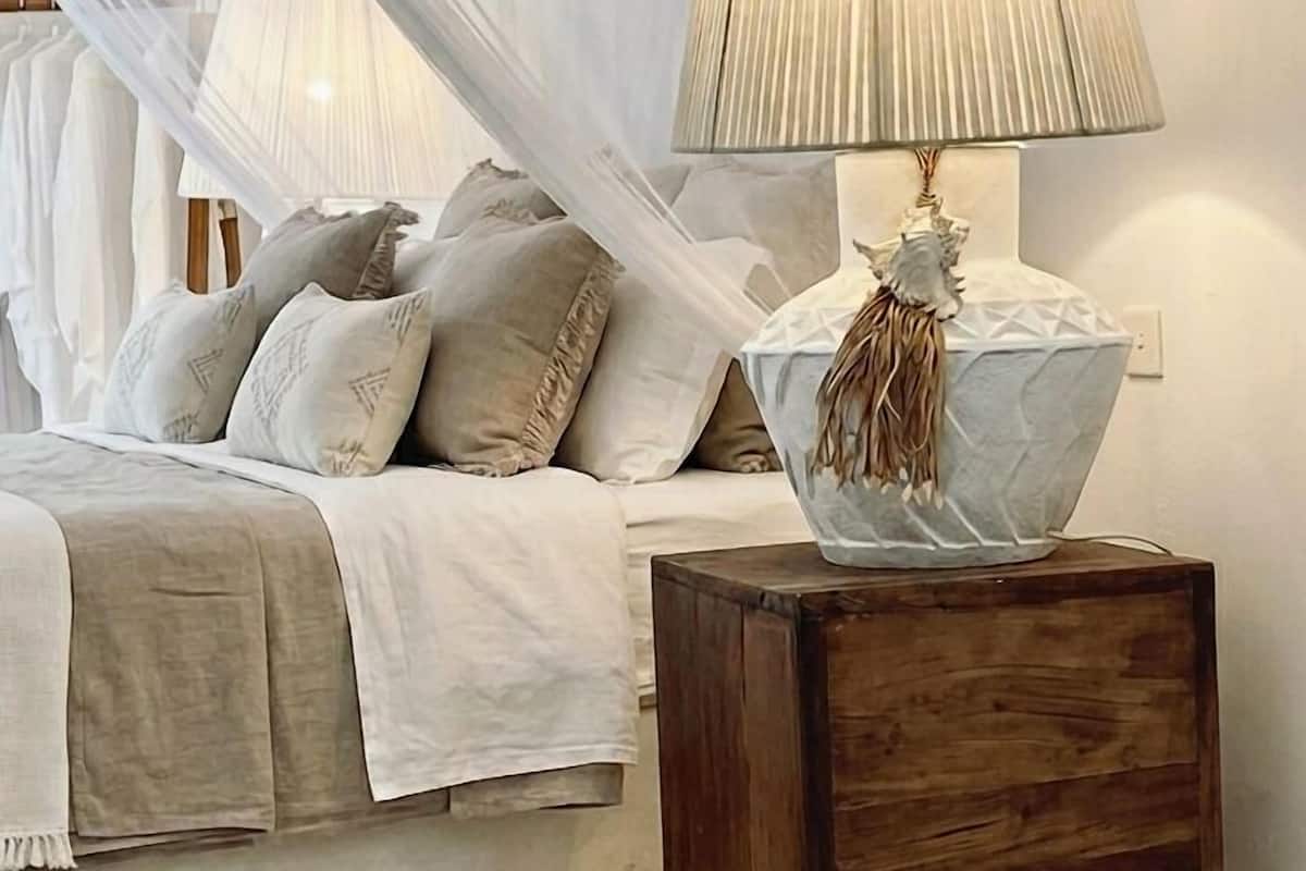 Quarto com cama, mesa de cabeceira, luminária e dossel.