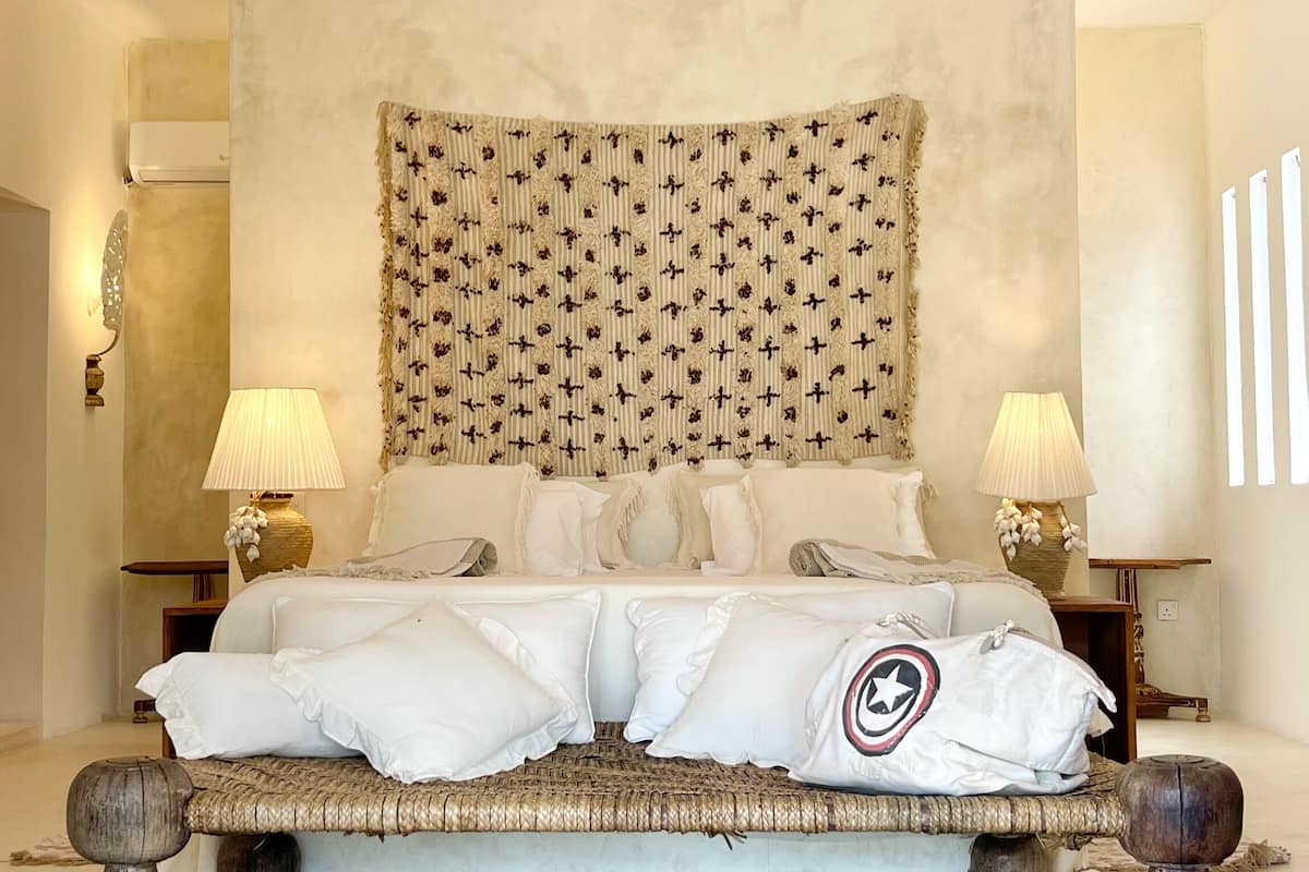Uma cama grande com cabeceira estampada, duas luminárias de mesa e um travesseiro decorativo com um símbolo de estrela.