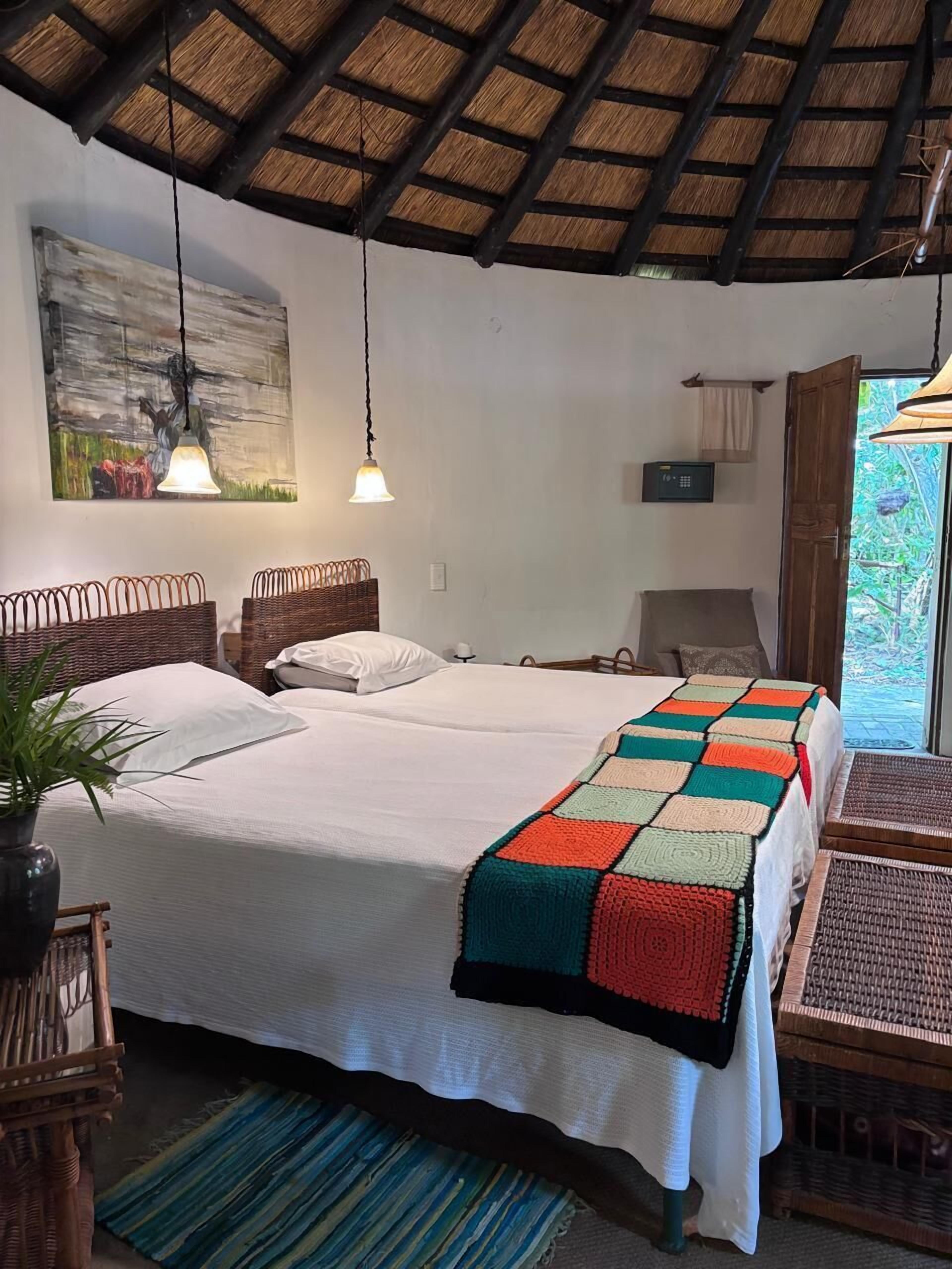 Quarto com cama, duas luminárias pendentes, um quadro, uma janela e uma porta.