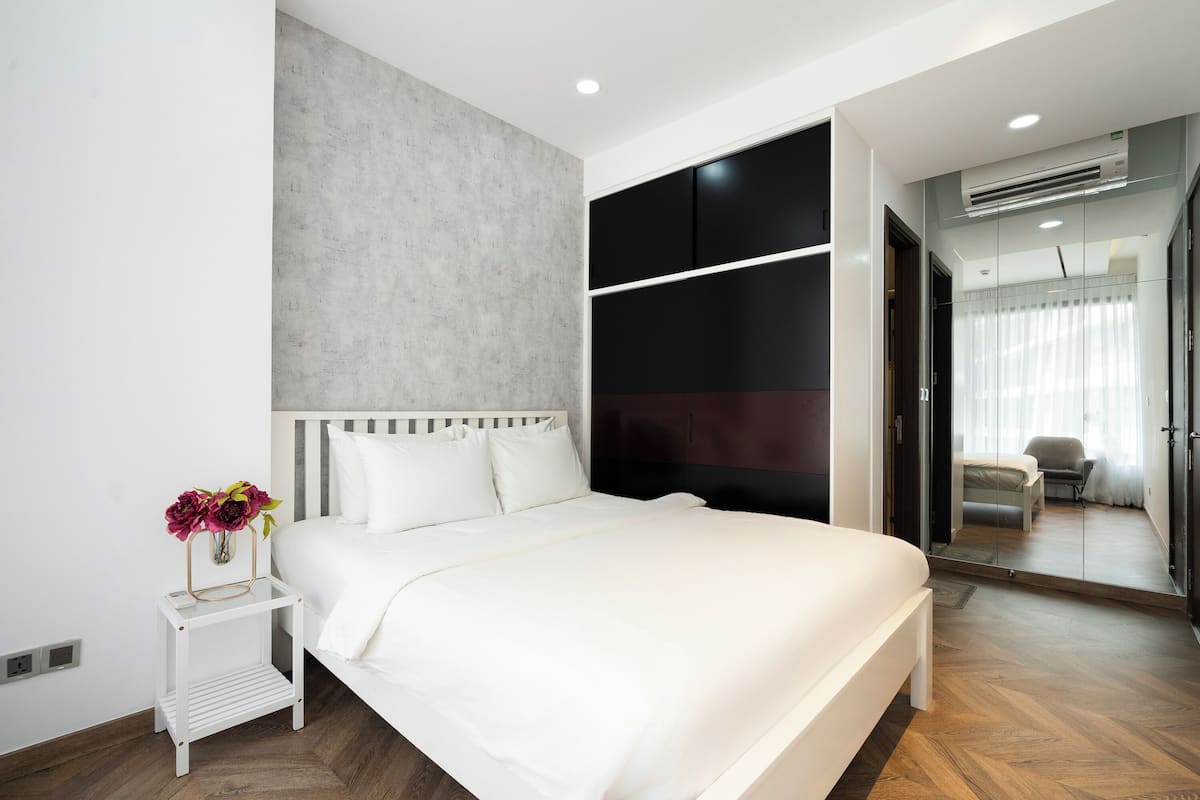 Quarto moderno com uma cama grande, mesa de cabeceira com um vaso, guarda-roupa e um espelho.