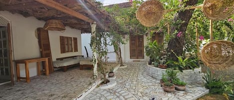 Pátio com piso de pedra, telhado de colmo, cestos de vime e plantas em vasos.