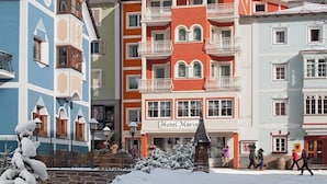 Hotel de vários andares com varandas, chão coberto de neve e céu claro.