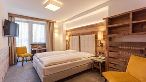 Quarto de hotel com uma cama, escrivaninha, cadeira, televisão e cabeceira de madeira.