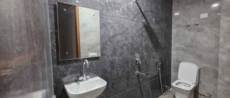 Uma casa de banho com lavatório, espelho, chuveiro e sanita.