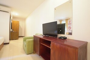 Quarto de hotel com escrivaninha de madeira, televisão, cadeira verde, cama, guarda-roupa e espelho.