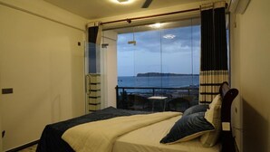 Quarto com cama, vista para o mar e varanda com cadeiras.