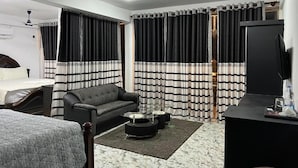 Quarto de hotel com cama, sofá, televisão, escrivaninha e cortinas.