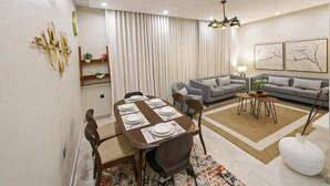 Uma sala de estar moderna com área de jantar, sofás cinzentos, um candelabro e obras de arte na parede.