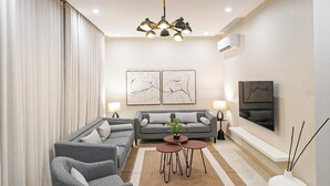 Uma sala de estar moderna com um conjunto de sofás, uma mesa de centro, uma televisão e obras de arte na parede.
