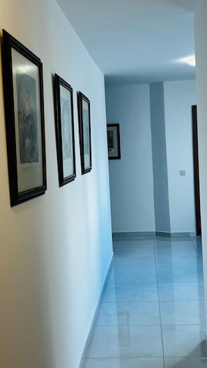 Um corredor com quadros nas paredes, chão de azulejos e uma porta no final.