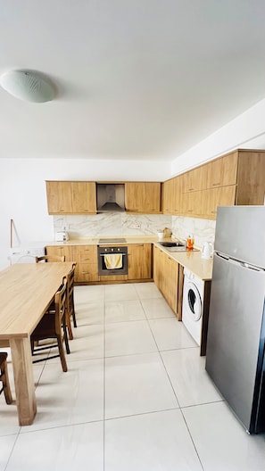 Cozinha moderna com armários de madeira, geladeira de aço inoxidável, forno embutido e máquina de lavar.