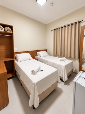 Quarto de hotel com duas camas, um guarda-roupa de madeira, uma mesinha e um espelho.