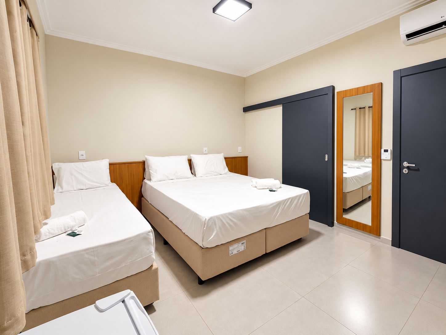 Quarto de hotel com duas camas, um guarda-roupa, um espelho e um aparelho de ar condicionado.