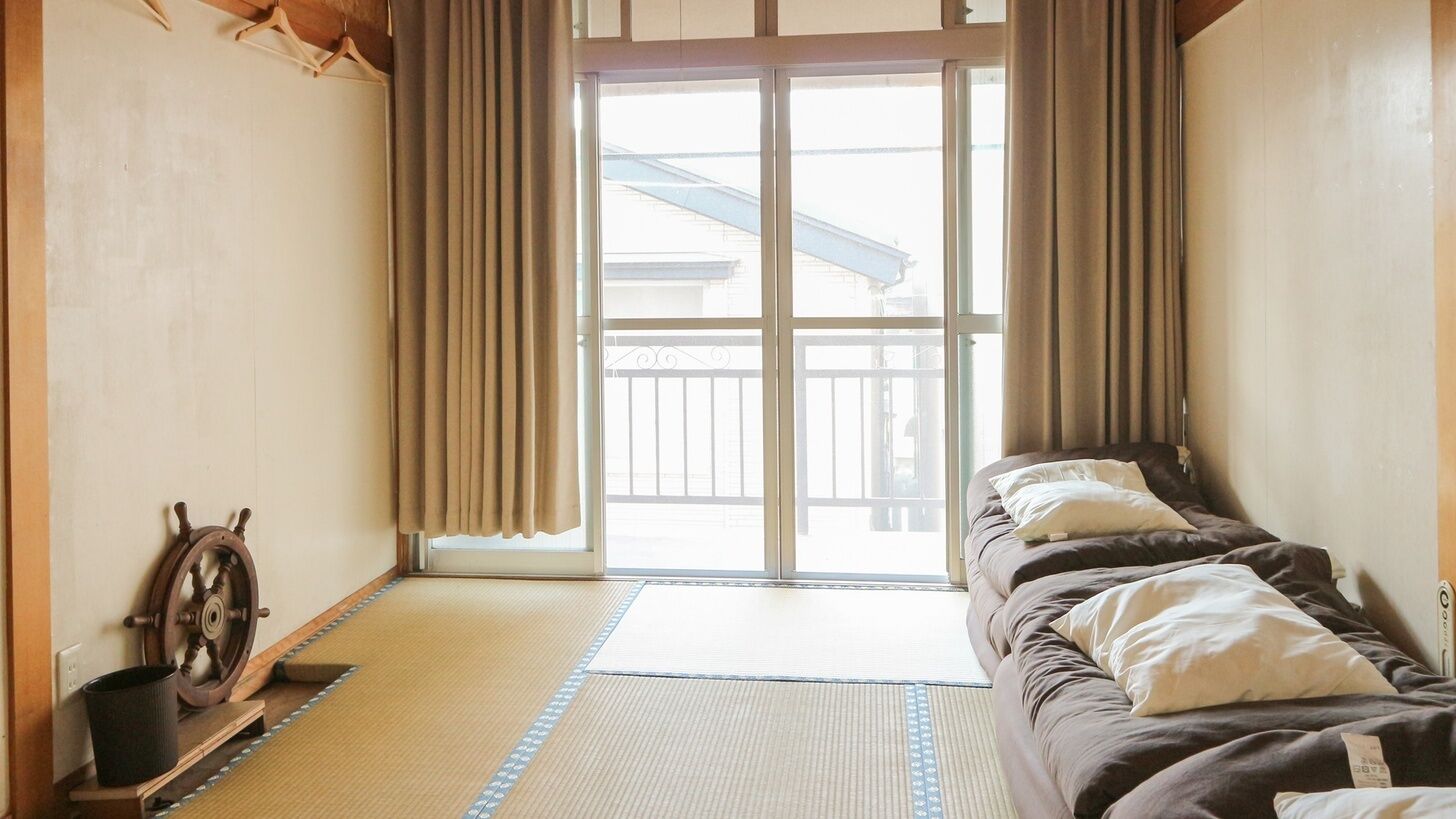Quarto com cama, tapete, leme de madeira e vista para uma varanda.
