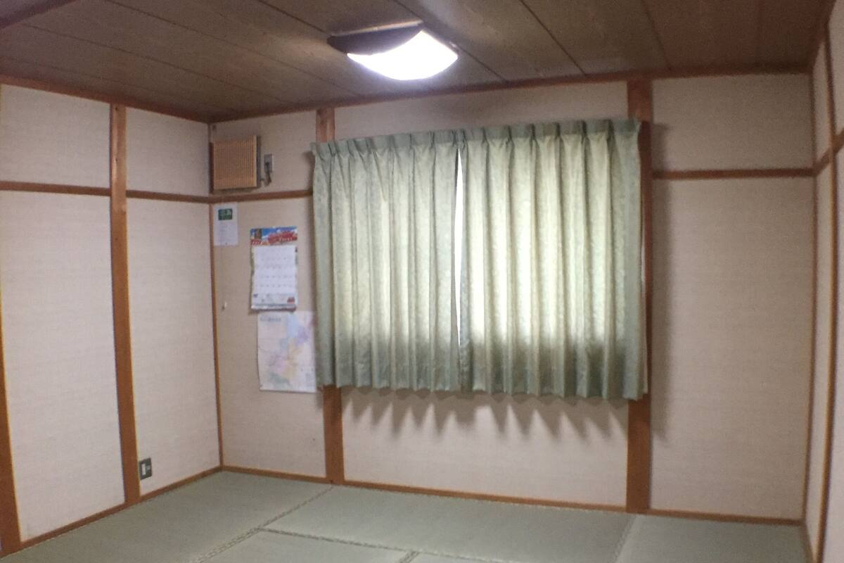 Um quarto com piso de tatame, um toldo deslizante, um ventilador de teto e uma janela com cortina.