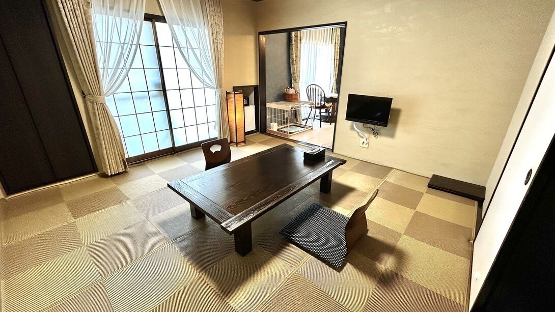Quarto japonês tradicional com tatames, uma mesa baixa, televisão e uma porta deslizante para um espaço adjacente.