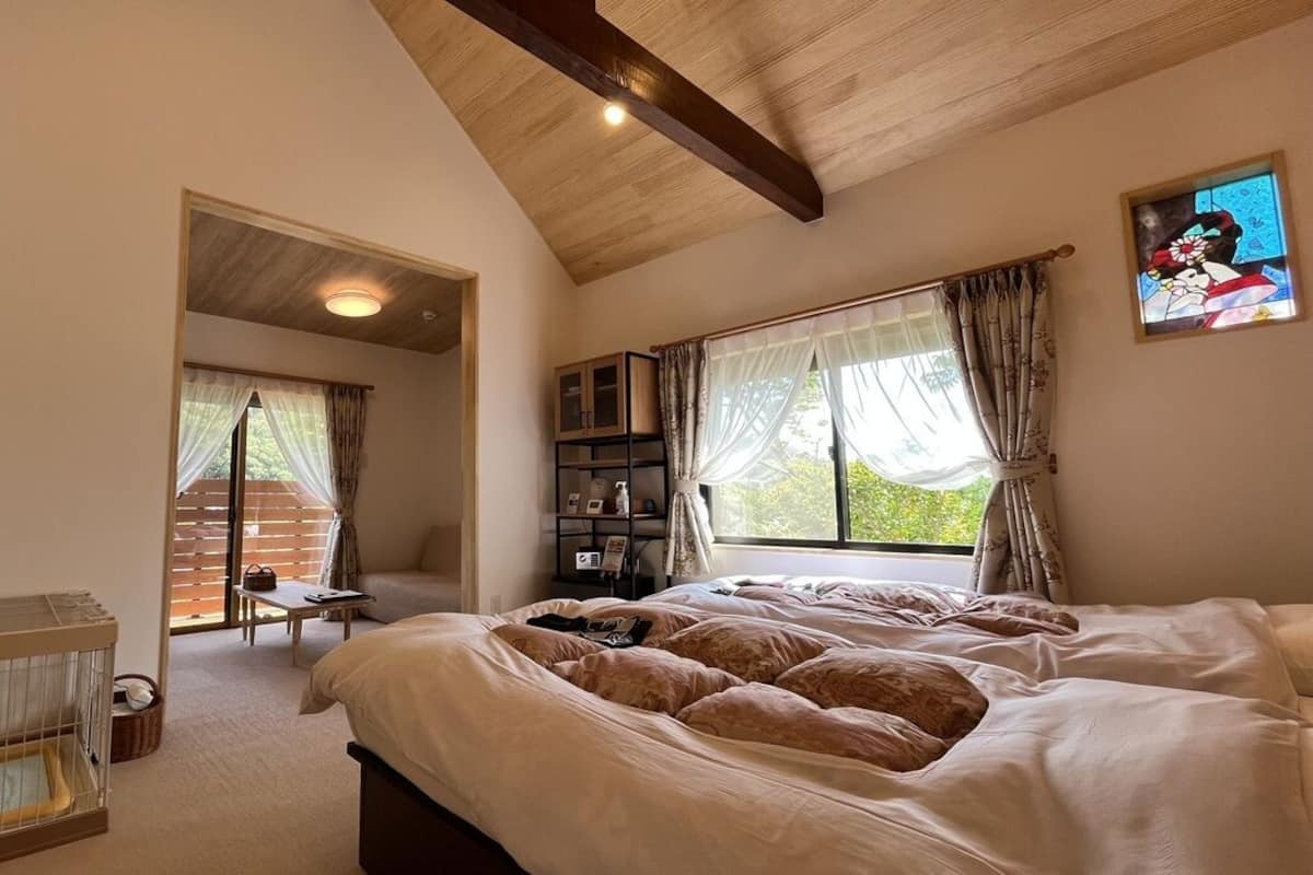 Quarto com cama, janela com cortinas, uma mesinha, armário e gaiola de animal de estimação.