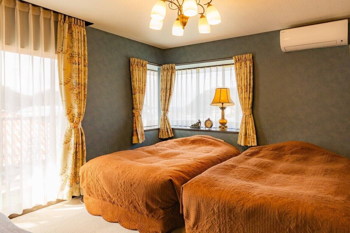 Quarto com duas camas, janela com cortinas, luminária e ar condicionado.