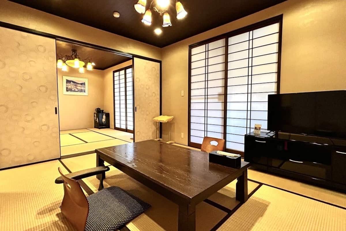 Quarto japonês tradicional com tatames, uma mesa baixa, televisão e portas deslizantes.
