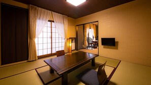 Um quarto japonês tradicional com tatames, uma mesa baixa, uma porta deslizante e uma televisão fixada na parede.