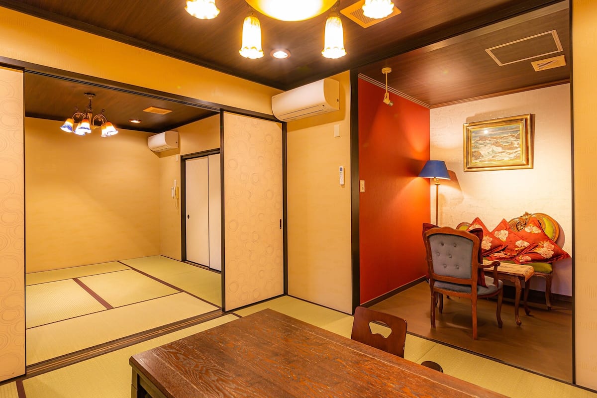 Um quarto japonês tradicional com tatames, uma mesa de madeira, uma cadeira, uma escrivaninha com uma luminária e um quadro na parede.