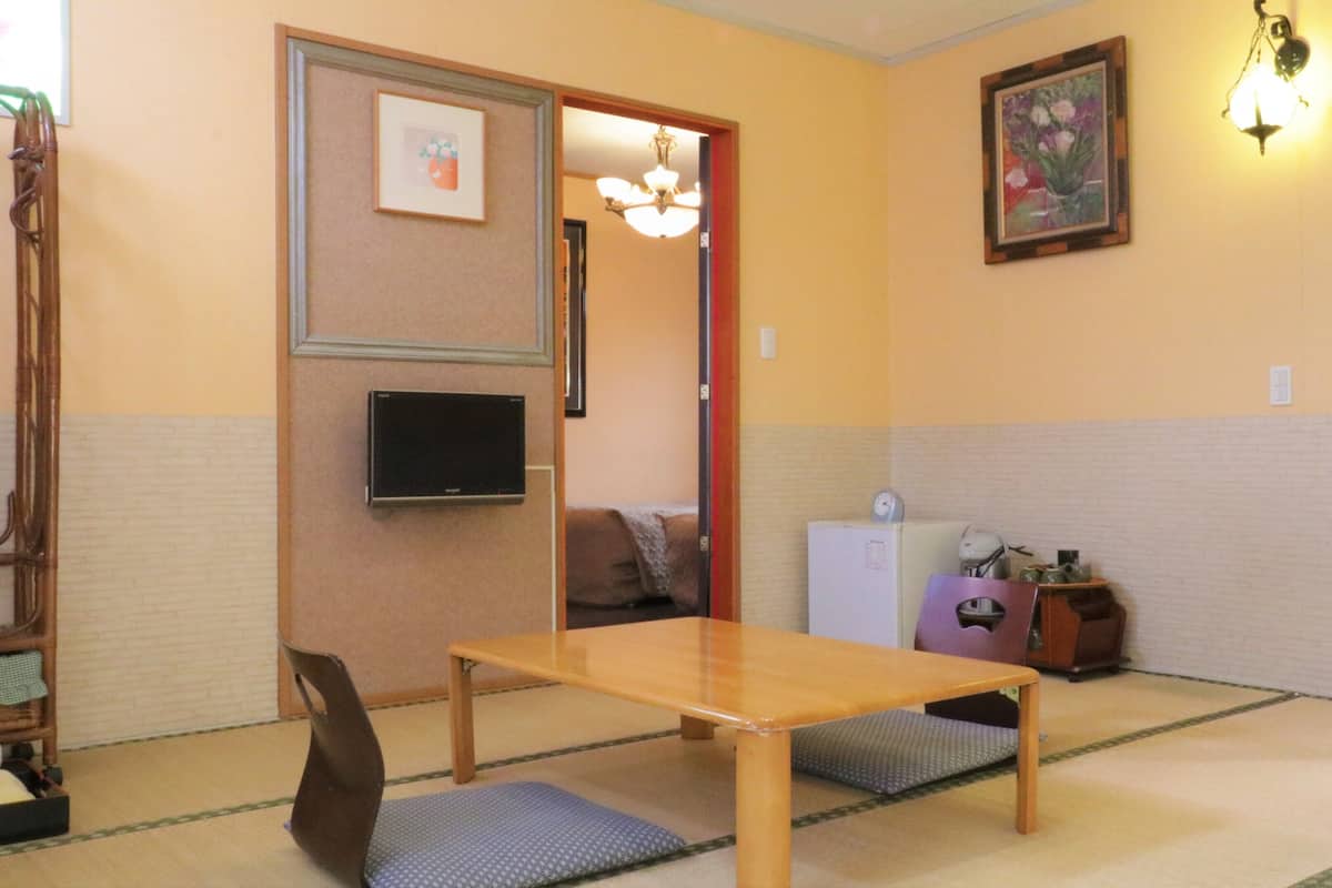 Um quarto em estilo japonês tradicional, com tatames, uma mesa de madeira baixa, uma televisão e um pequeno frigorífico.