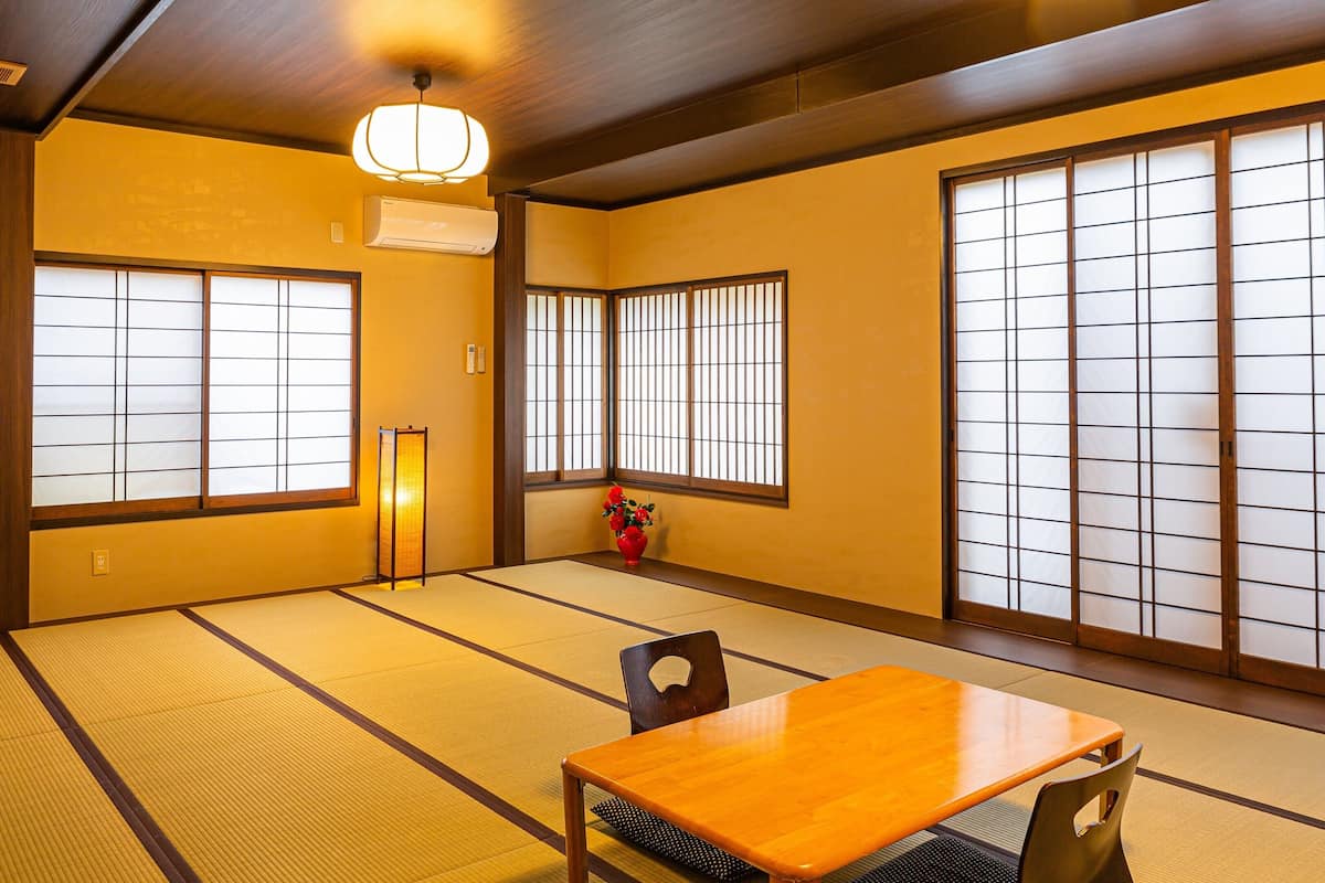 Um quarto japonês tradicional com tatames, biombos shoji, uma mesa de madeira e um vaso vermelho com flores.