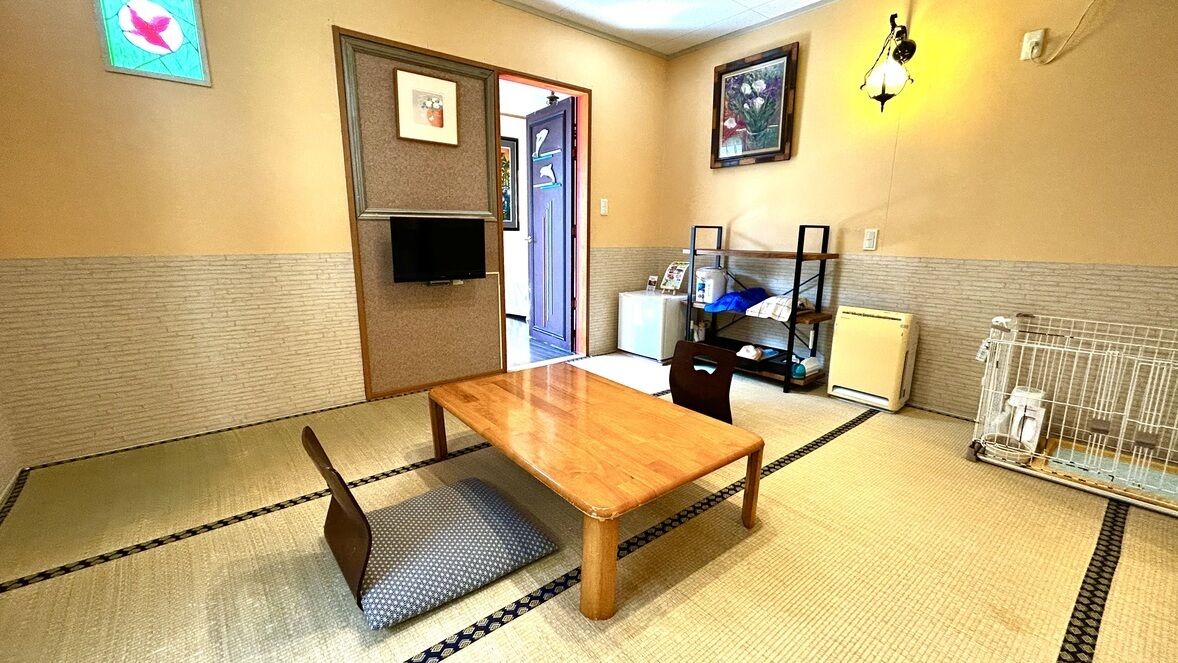 Um quarto com piso de tatame, uma mesa de madeira, uma televisão, um radiador e uma gaiola de pássaro.