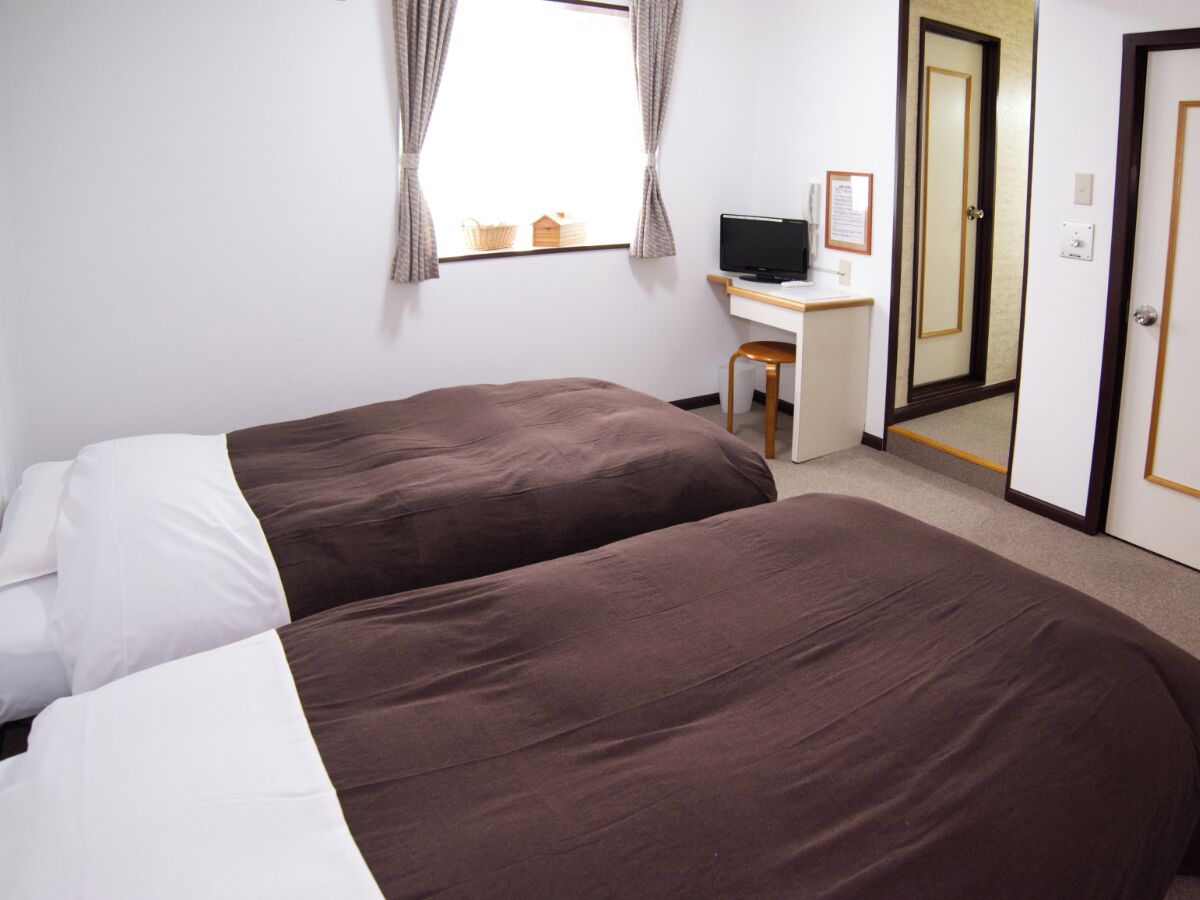 Quarto de hotel com duas camas, uma escrivaninha, uma televisão e um espelho.