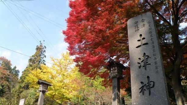 Um monumento de pedra com caracteres japoneses, um lança-luz tradicional japonês e uma ponte de madeira.
