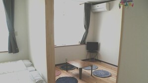Quarto com cama, uma mesinha, televisão e janela com cortinas.