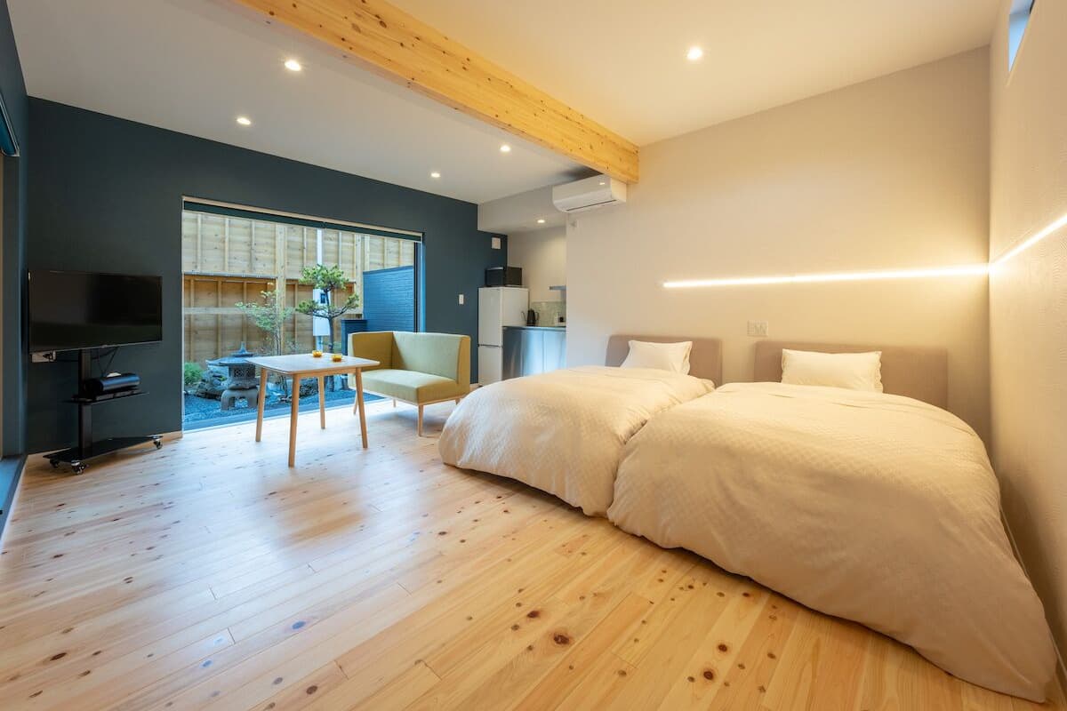 Quarto moderno com uma cama grande, uma TV, uma mesa de jantar e vista para um jardim.