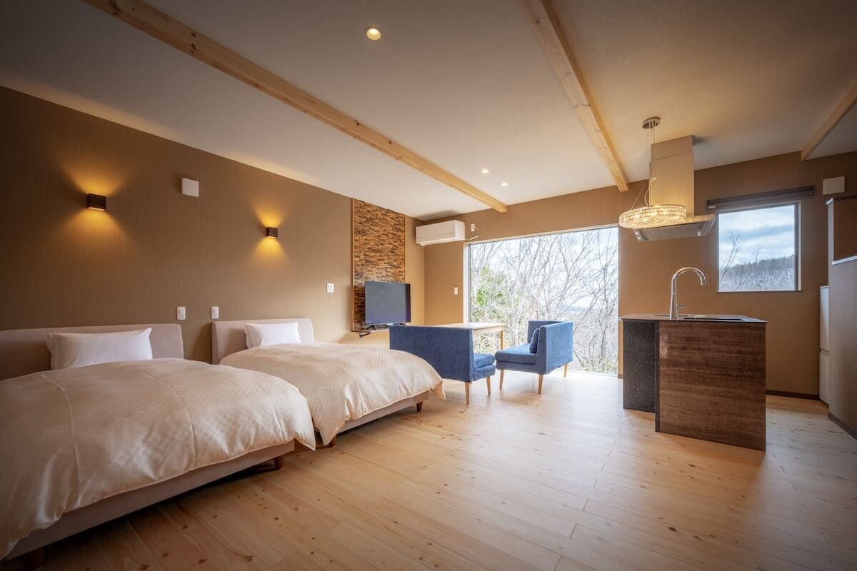 Quarto moderno com duas camas, um pequeno espaço de estar e bancada de cozinha.