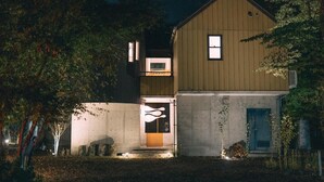 Uma casa de dois andares com fachada de concreto, uma porta visível e uma pequena janela.