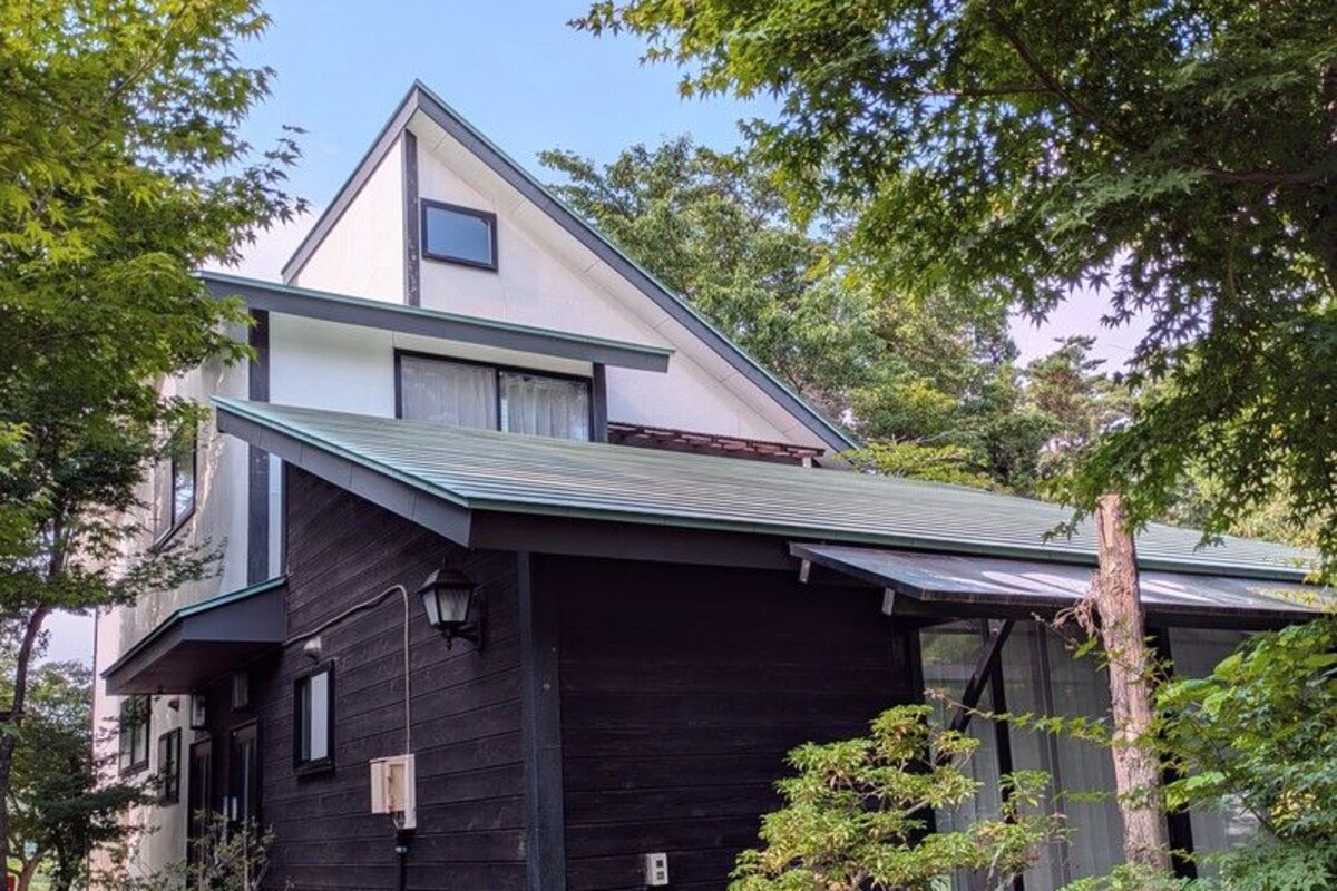 Uma casa moderna de dois andares com fachada escura, telhado inclinado e garagem visível.